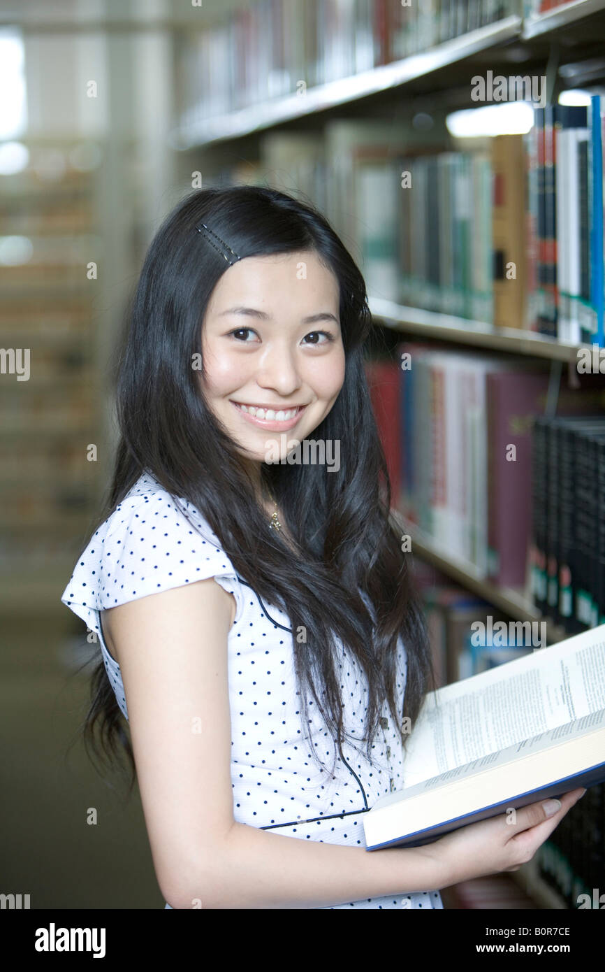 Portrait of young woman in library holding book Stock Photo - Alamy
