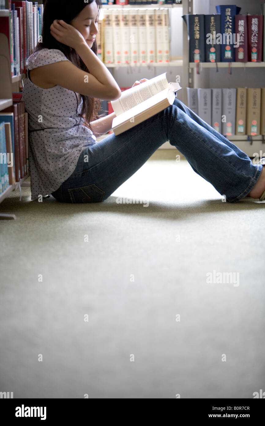 Young woman sitting on floor in library reading book Stock Photo - Alamy
