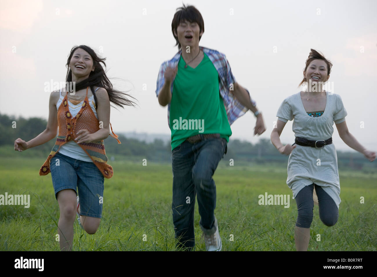 Three young people running across meadow Stock Photo - Alamy