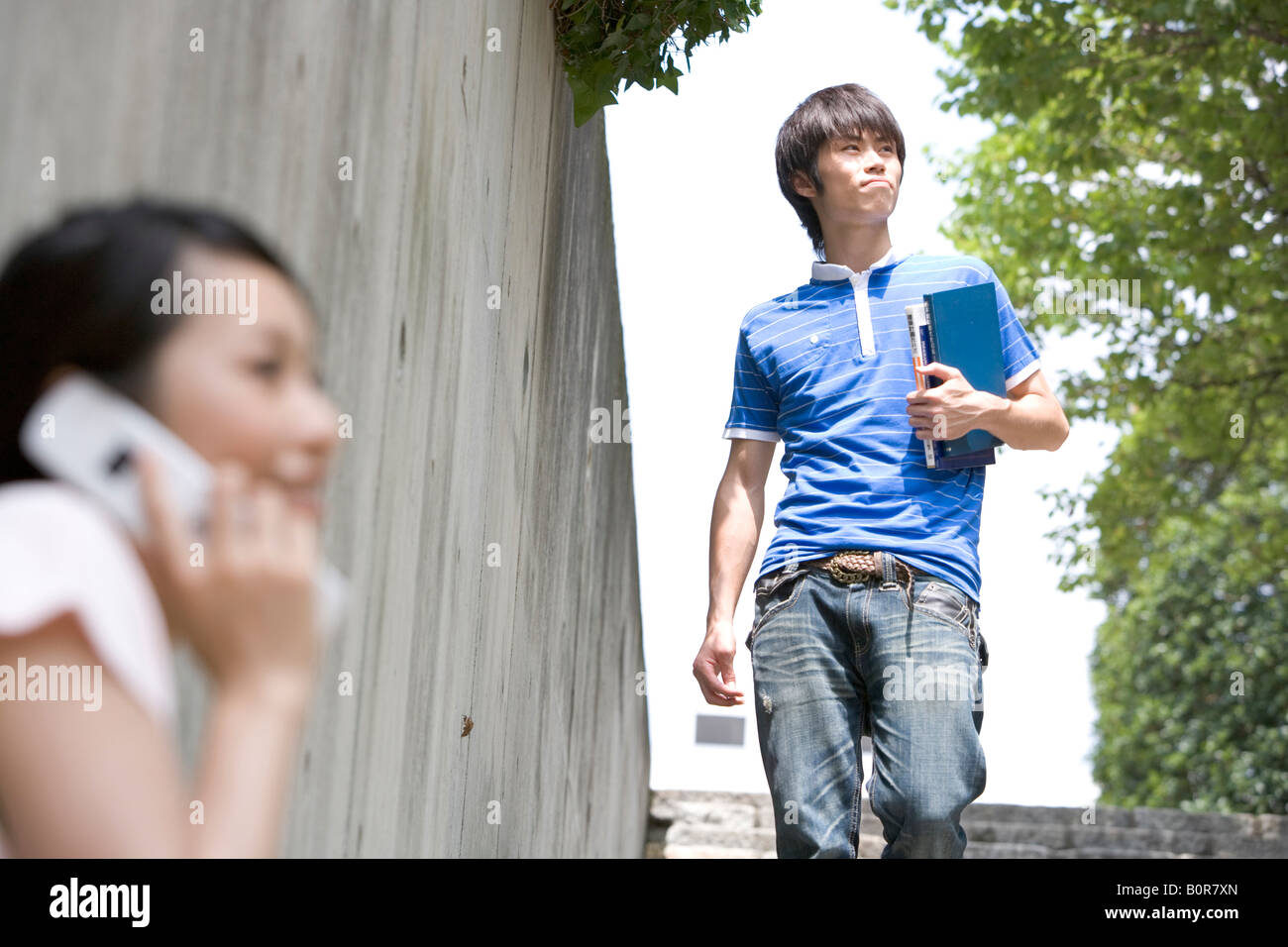 Teenage boy walking down steps with teenage girl talking in mobile ...