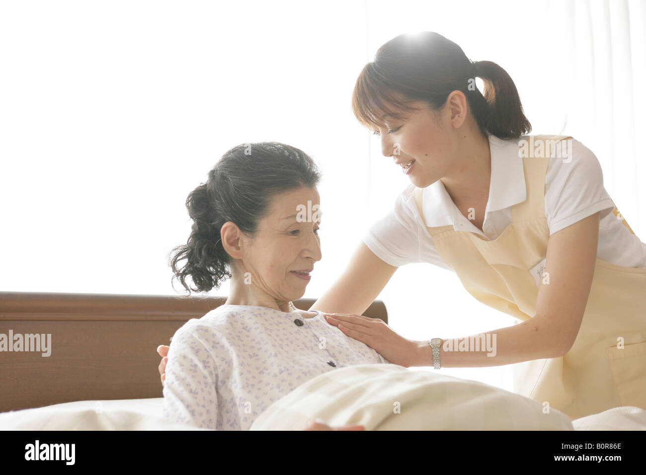 Female nurse helping elderly woman to lay down in bed Stock Photo - Alamy