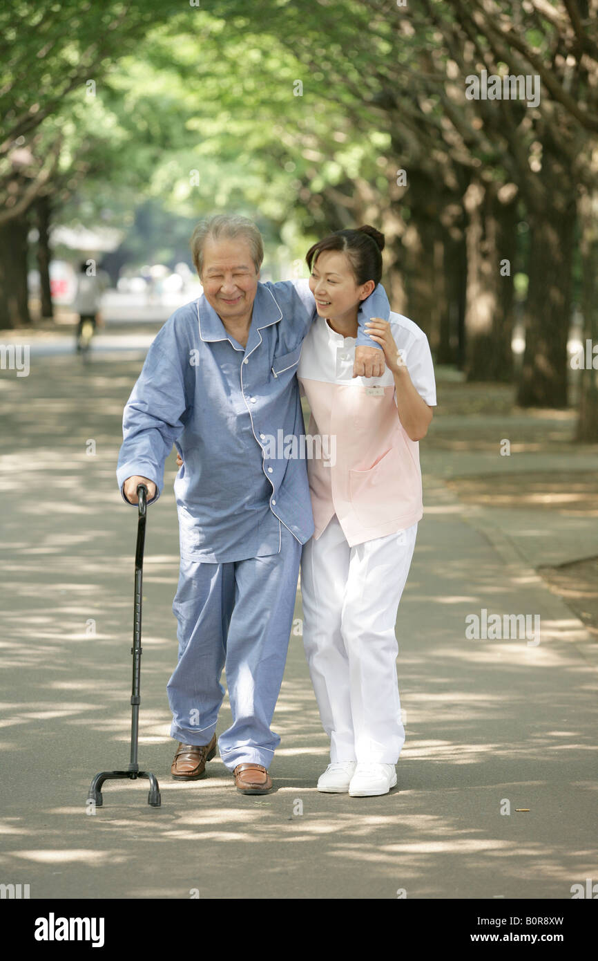 Female nurse supporting senior man walking with cane in park Stock ...