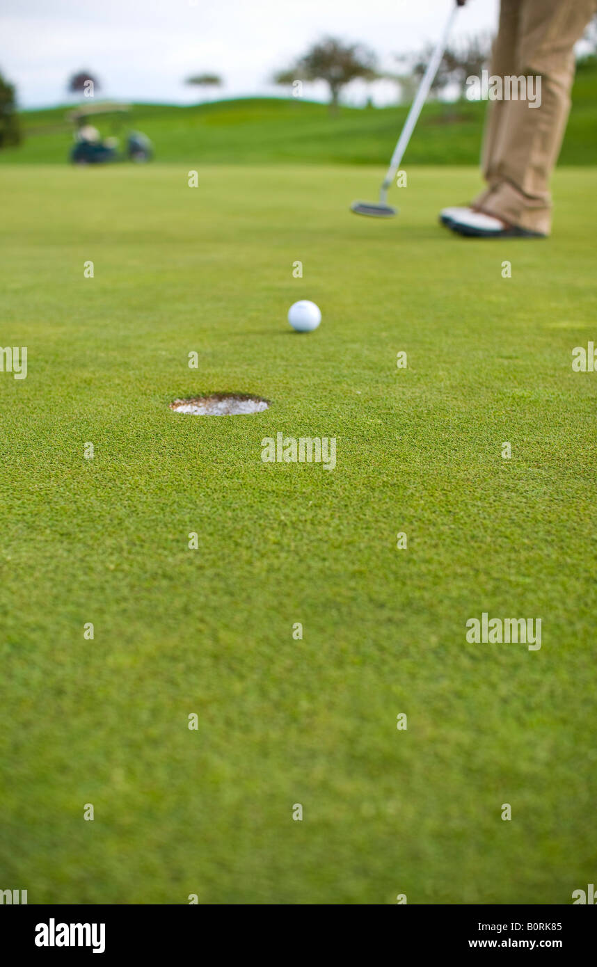 A golfer putting into a hole on a putting green Stock Photo - Alamy