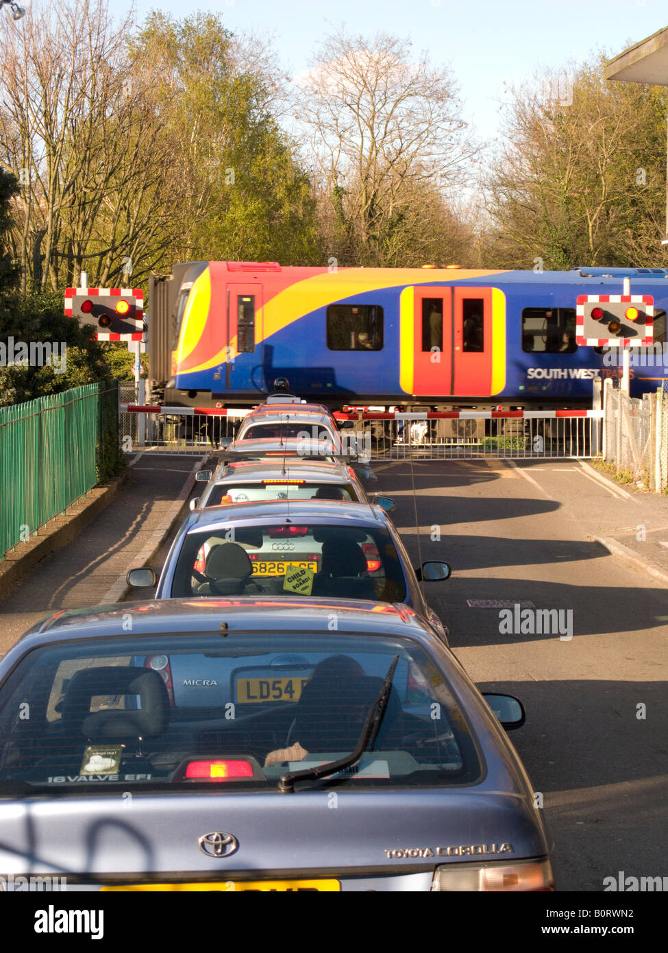 Cars wait at a railway level crossing barrier as train passes through ...