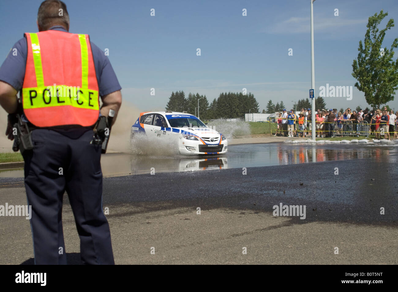 A police officer looks on as a Mazda rally car crosses a water splash ...