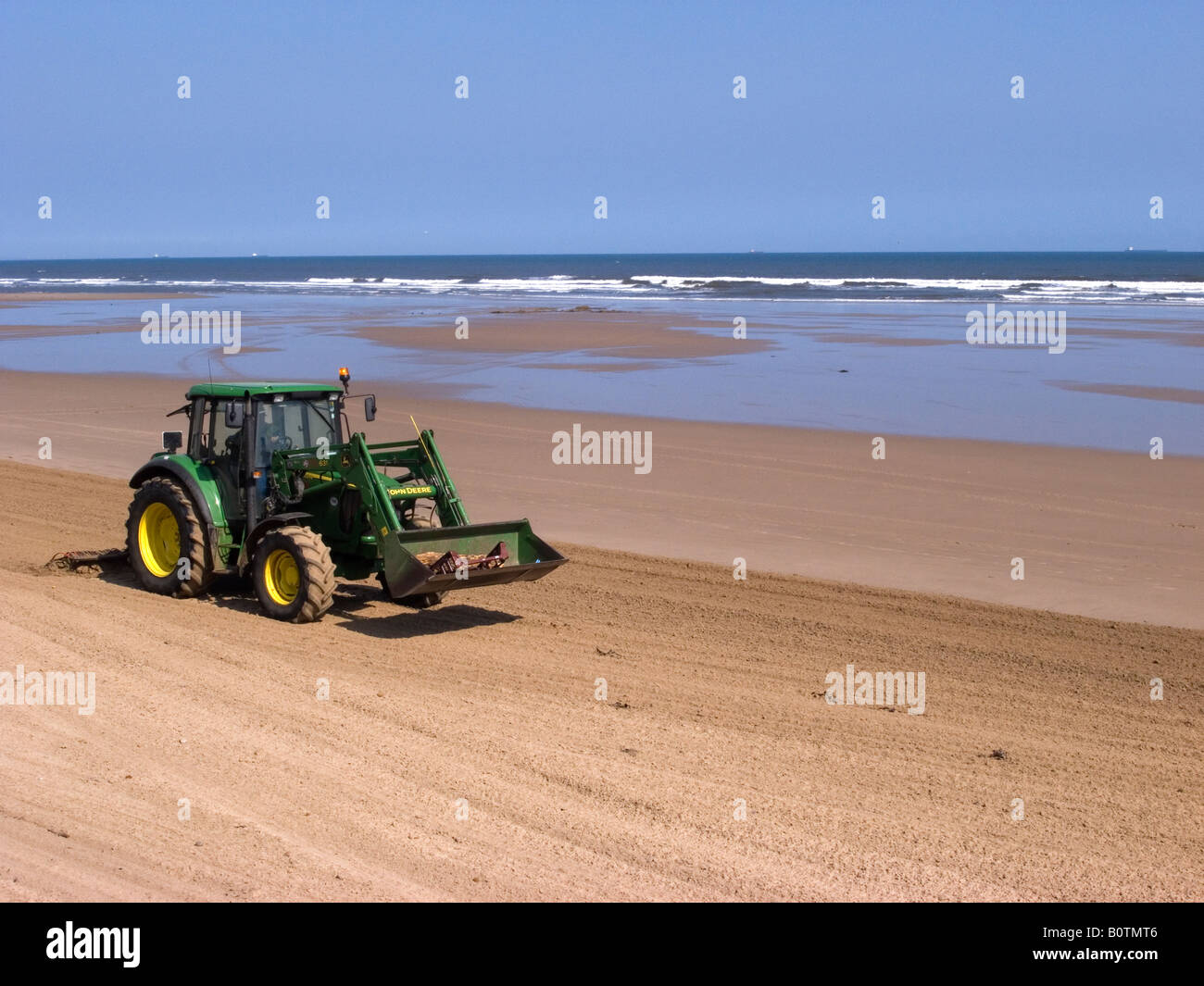 Tractor with rake and front loader being used to clean the sandy beach ...