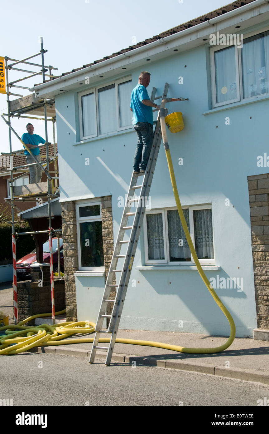 man on ladder Installing cavity wall rock wool insulation in a house to ...