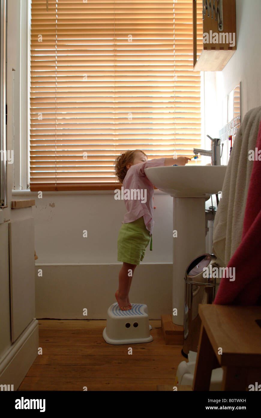 A toddler girl stretching up to the sink, trying to clean her teeth ...