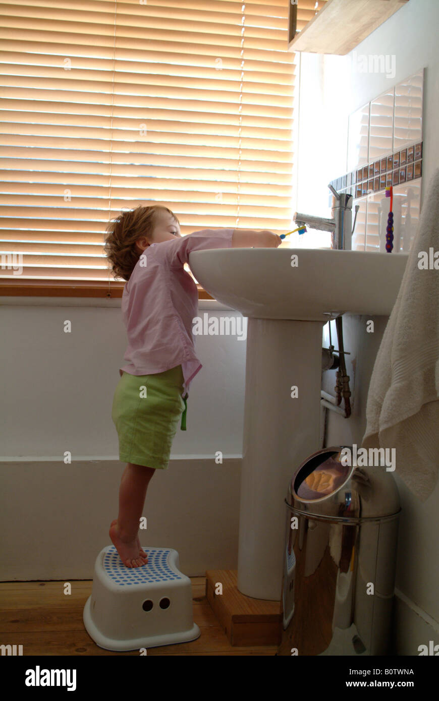 A toddler girl stretching up to the sink, trying to clean her teeth ...