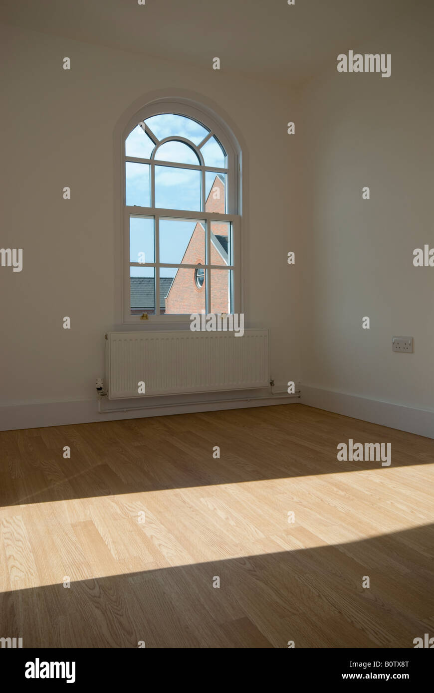 bare room with arched window, radiator and wooden floor with sunlight ...