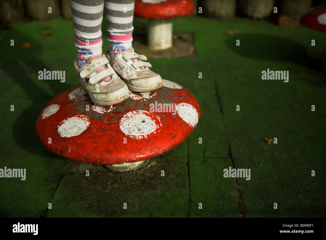 Girl aged four steps across concrete toadstools in a public park ...