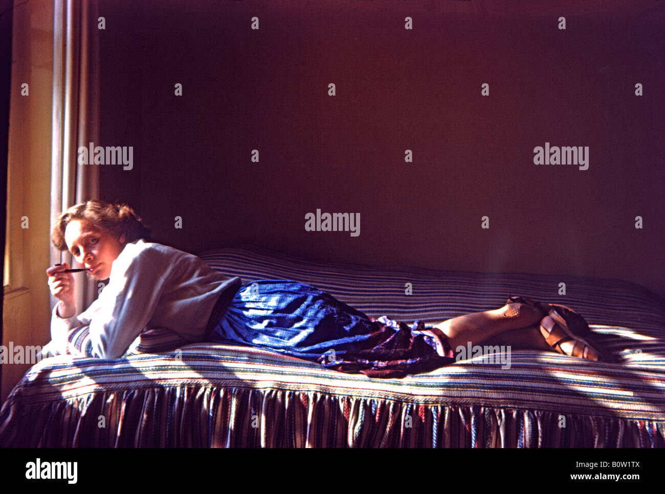 young woman smoking pipe lying on divan covered with folk weave ...
