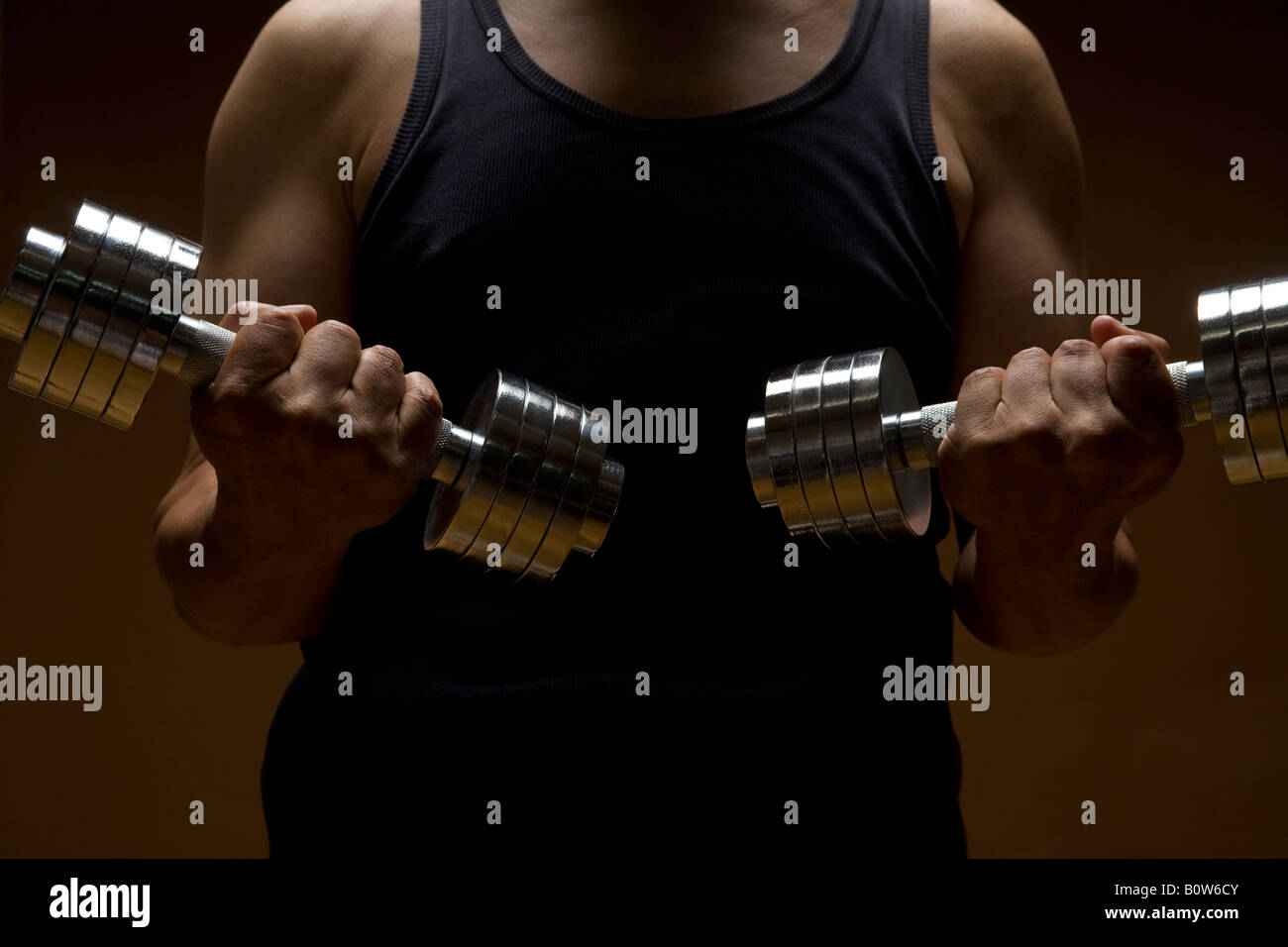 Muscular man holding dumbbells, midsection Stock Photo - Alamy