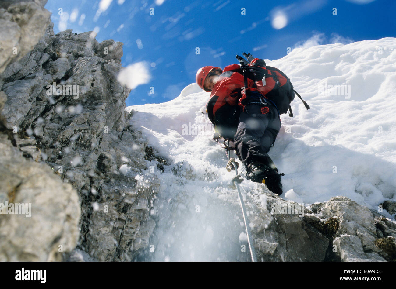 Female mountain climber climbing over a cornice on a steel rope, snow ...