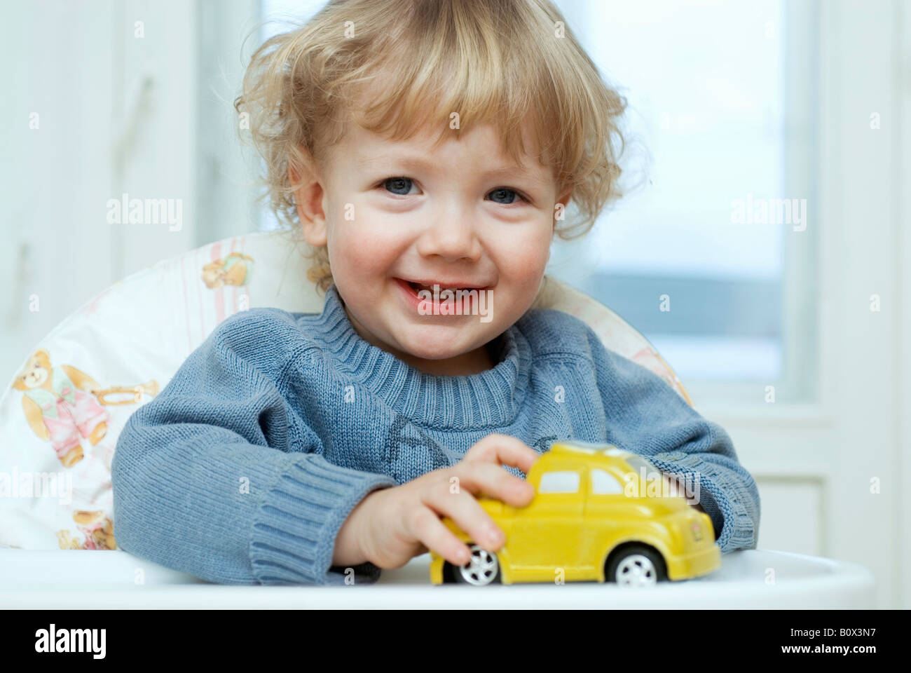 A young boy sitting in a high chair playing with a toy car Stock Photo ...