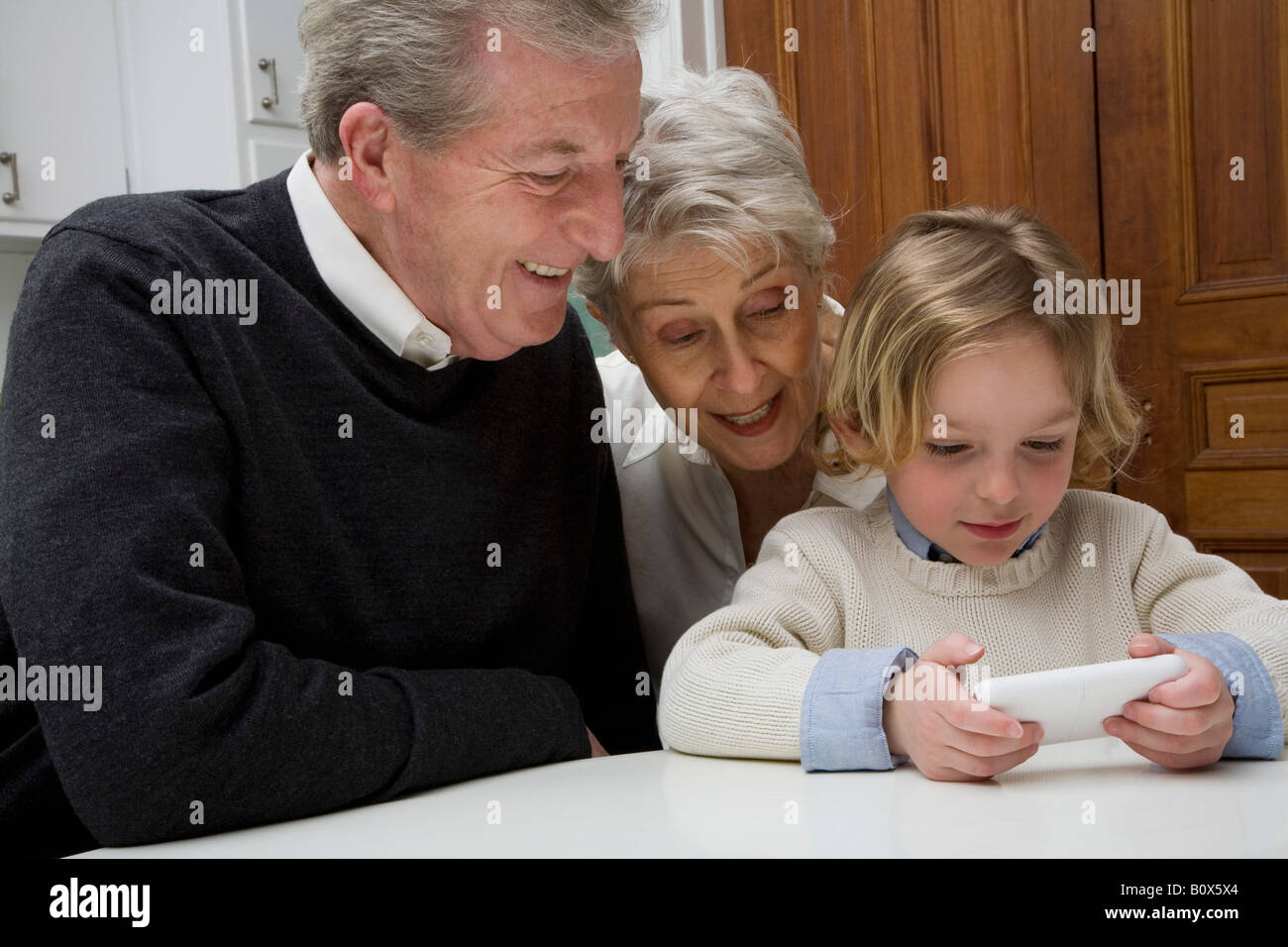 A grandson using a electronic device while his grandparents watch Stock ...
