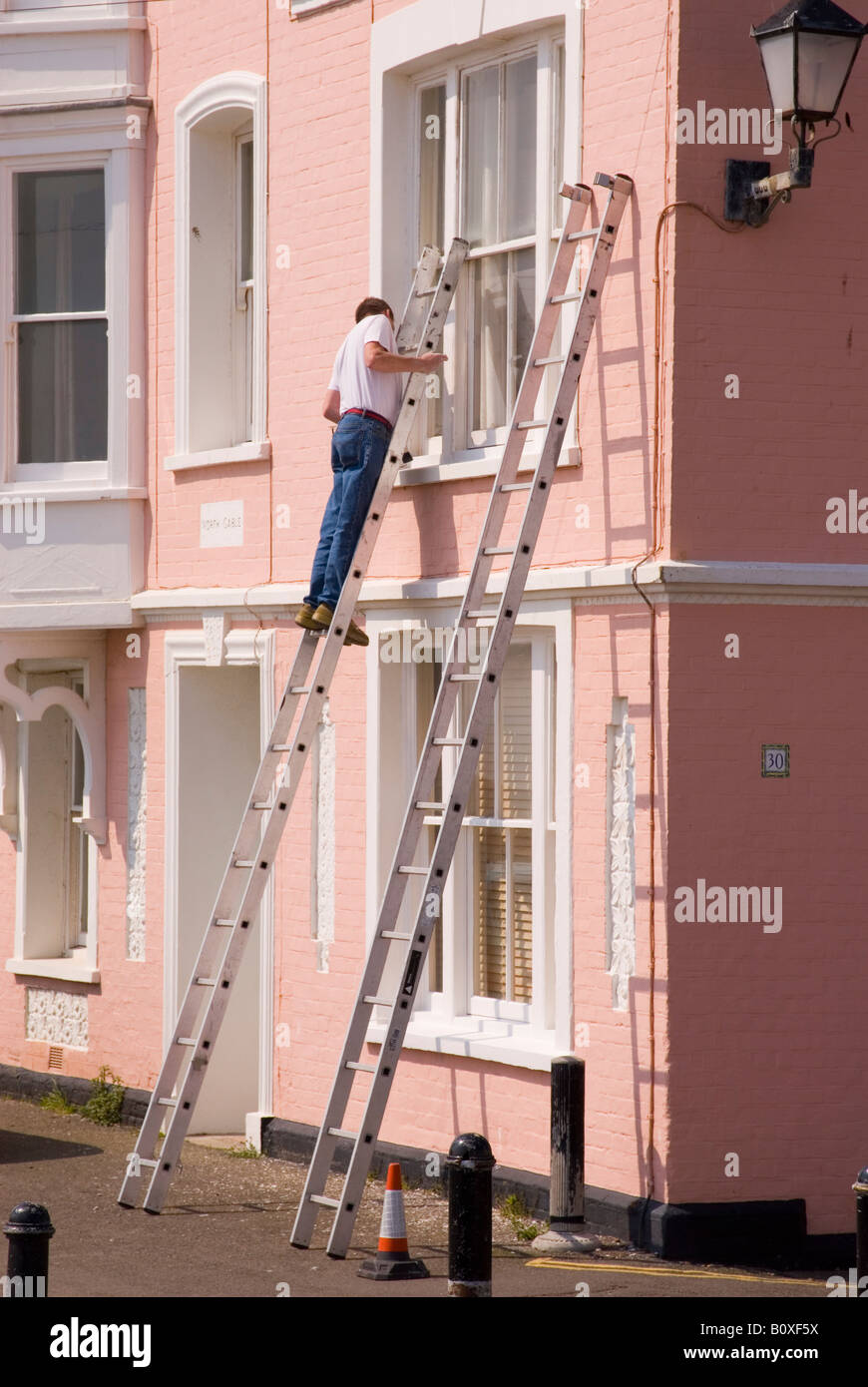 Man Painting Window On House Up Ladder in the uk Stock Photo - Alamy