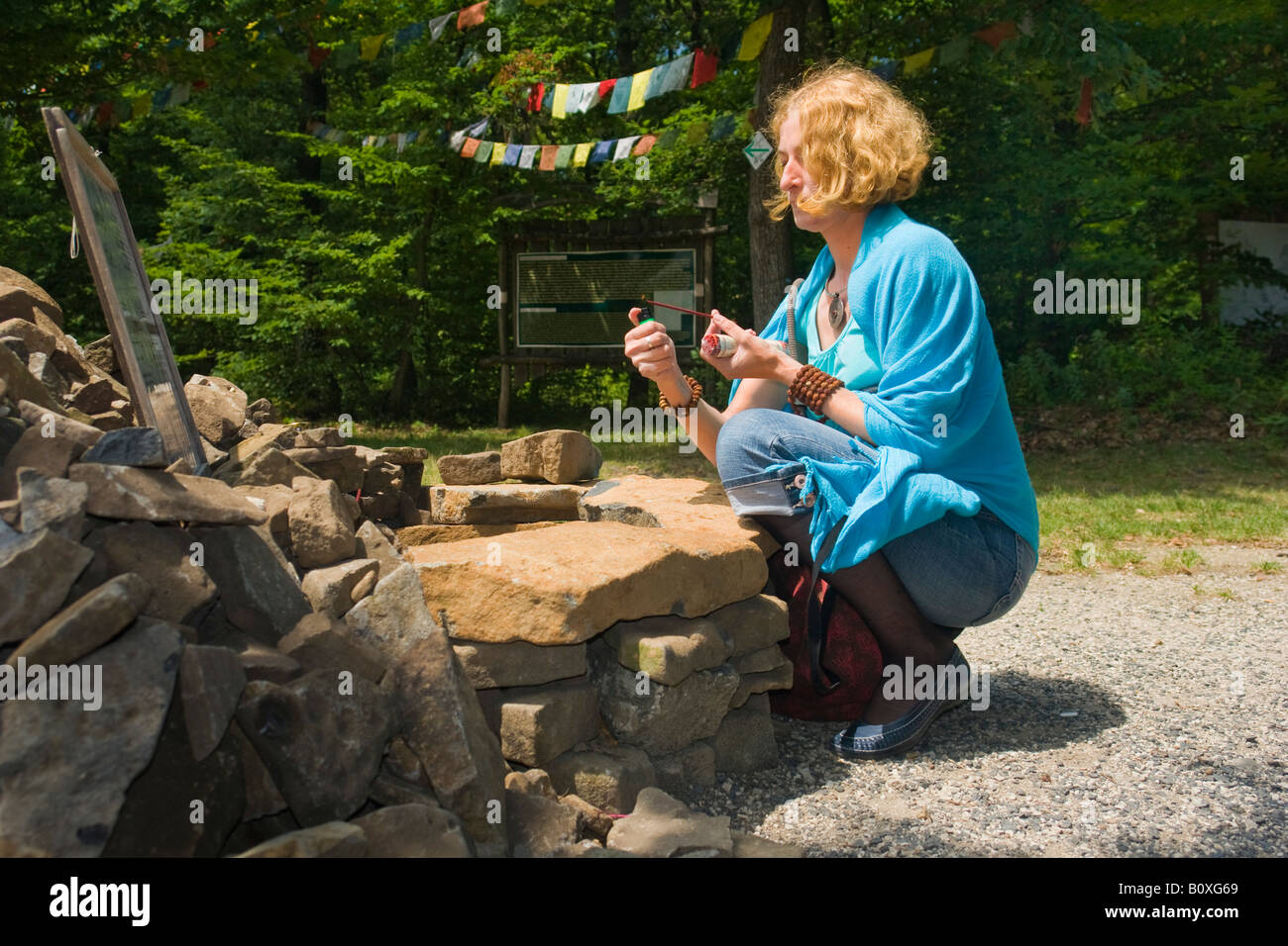 A woman offering incense on a small stone altar near a tibetan buddhist ...