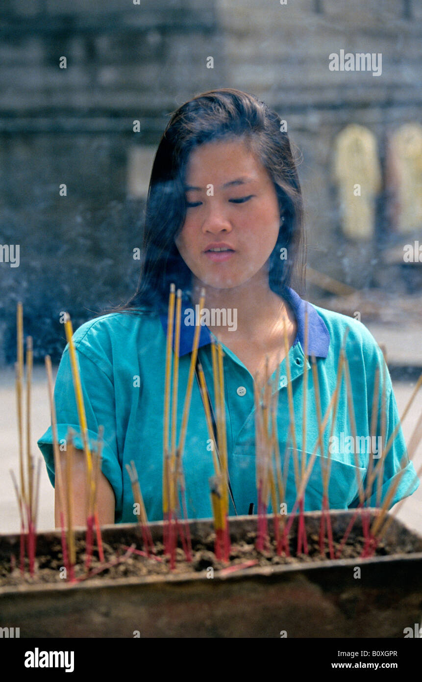 A young Chinese woman lights joss sticks or incense sticks at a public ...