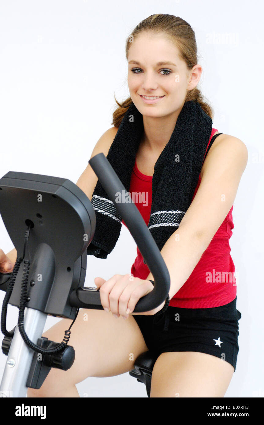 young woman in red sport shirt, sitting on an exercise machine, with a ...