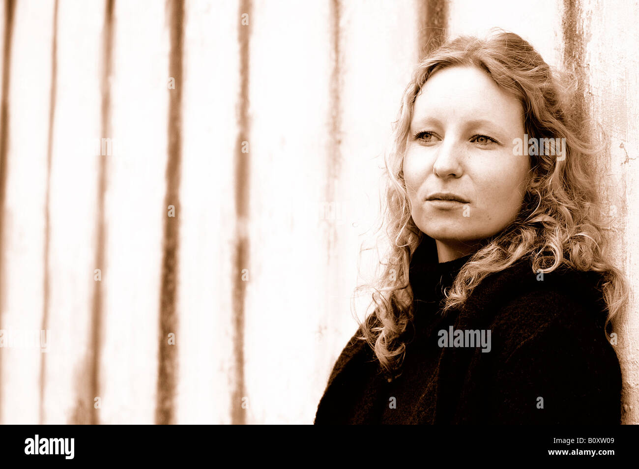 portrait of a fair- haired women with curly hair in front of a wall ...