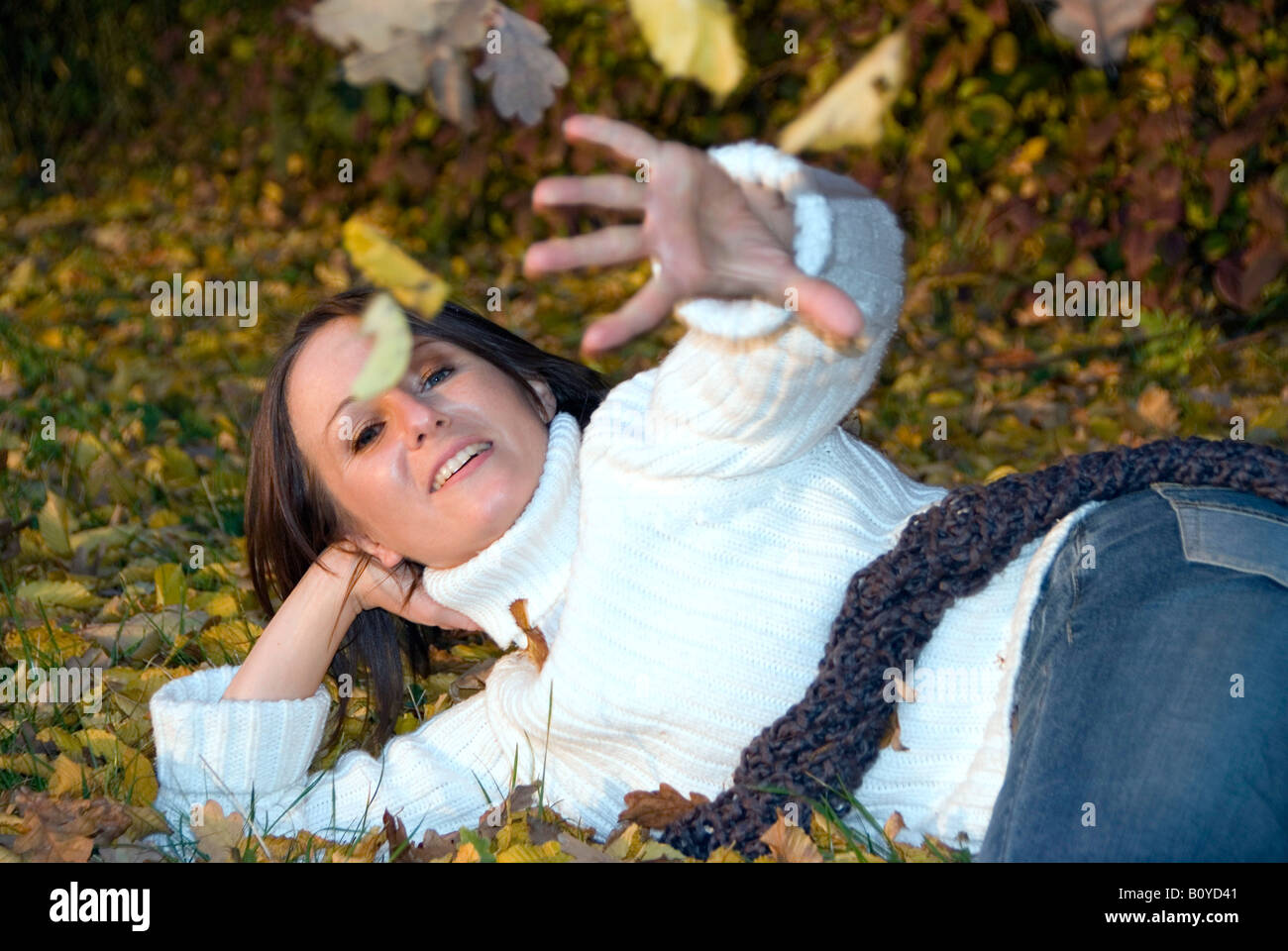 young woman in a white pully, lying and throwing with autumn foliage ...