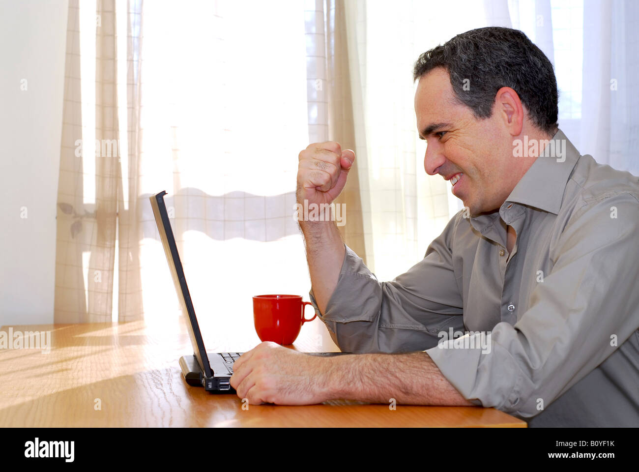 Man sitting at a desk and looking into his computer showing happiness ...