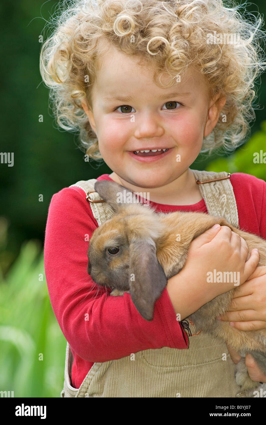 Blonde girl (4-5) with curly hair holding rabbit, portrait Stock Photo ...
