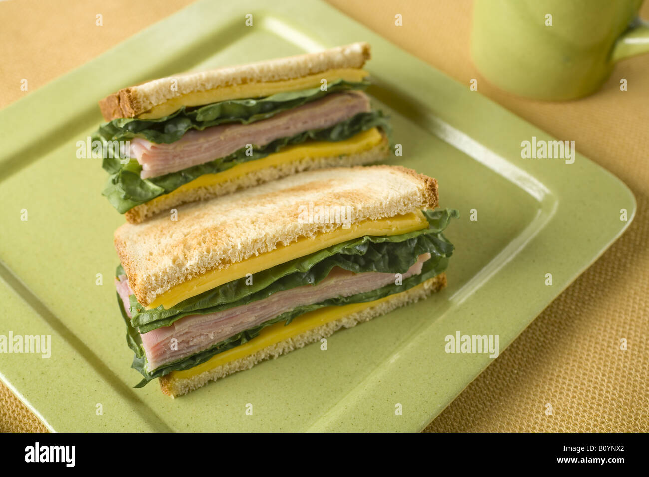 Stacked ham and cheese sandwich with spinach served on green square ...