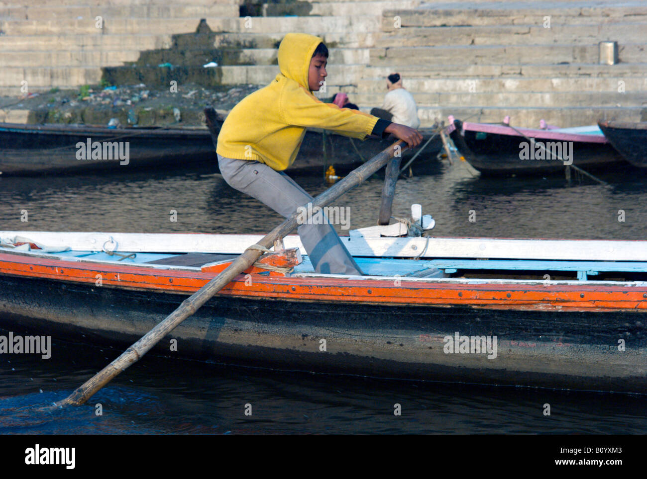 INDIA VARANASI Very young Indian boy uses all of his strength to row a ...