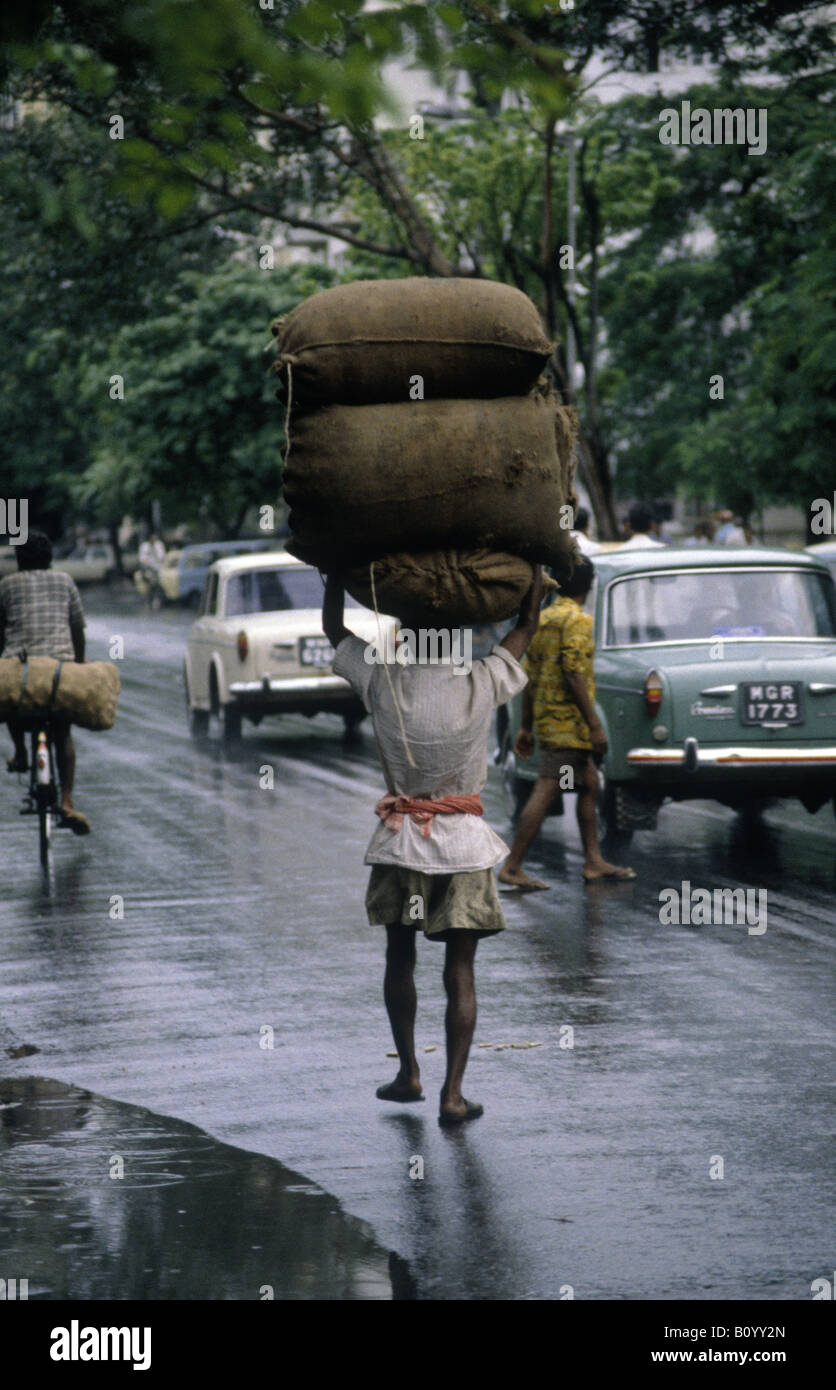 Man walking away from camera balancing heavy load of full sacks on head ...