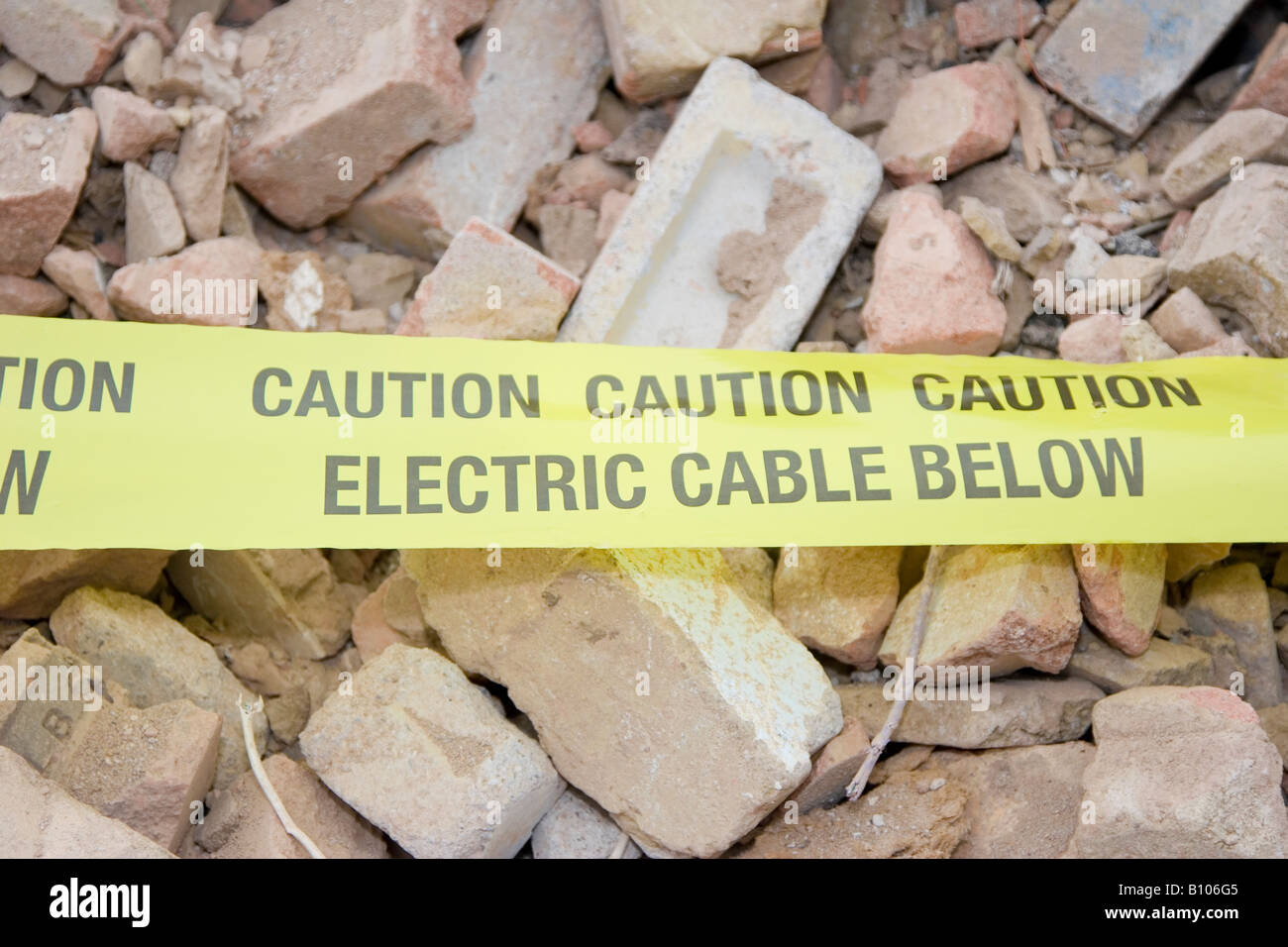 Electric cable caution warning tape across pile of bricks and rubble ...