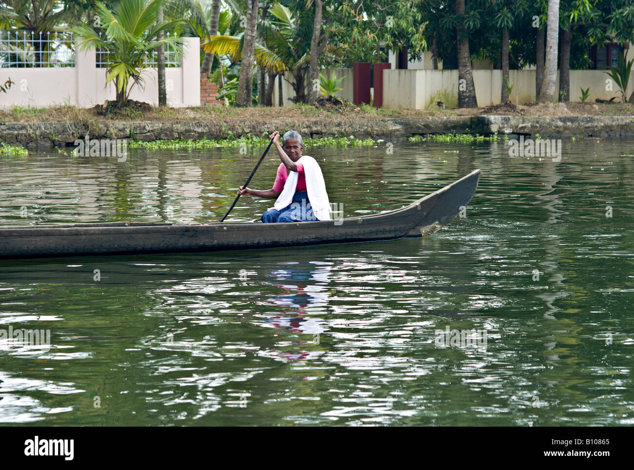 INDIA KERALA Elderly Indian woman rowing her wooden canoe down the ...