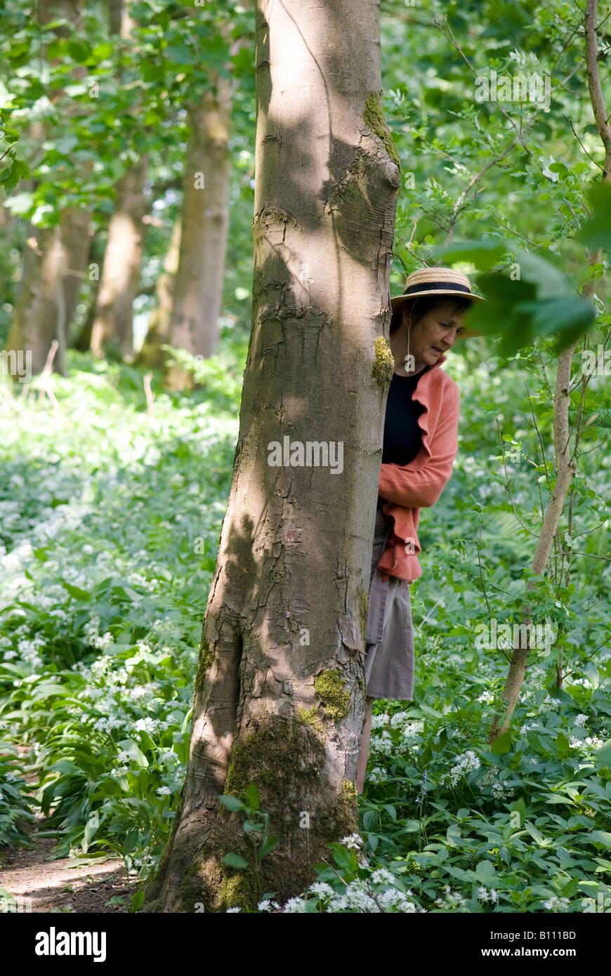 smartly dressed woman in straw hat looking around tree in woodland ...