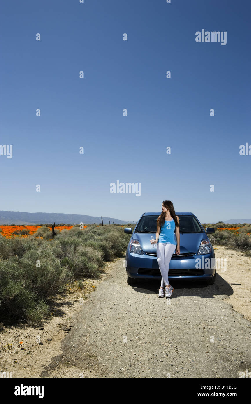 Young woman leaning against front of blue Toyota Prius on dirt road ...