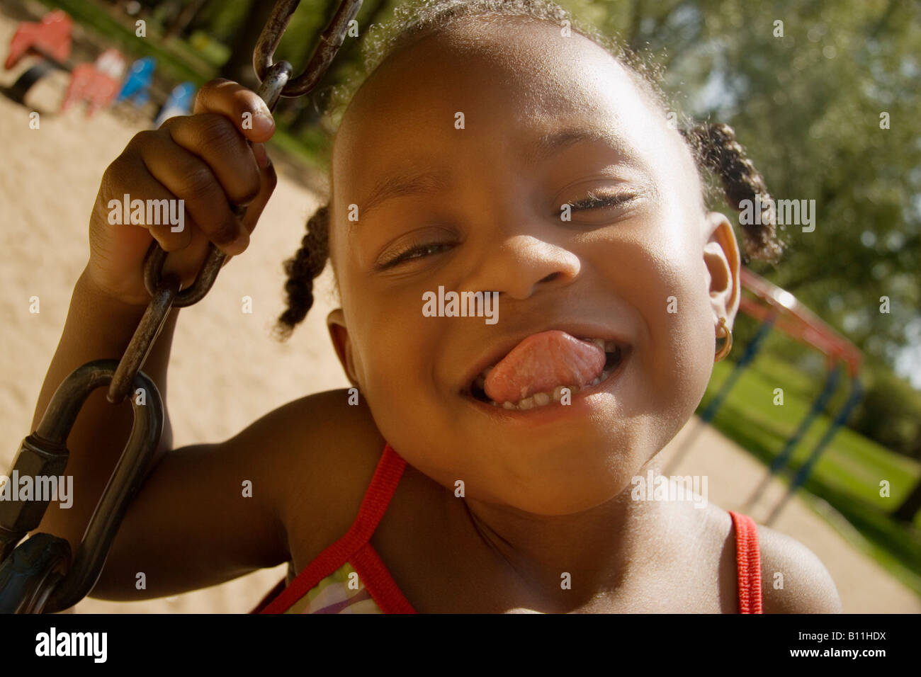 Young Girl Sticking Out Her Tongue While On The Swingset In The Park