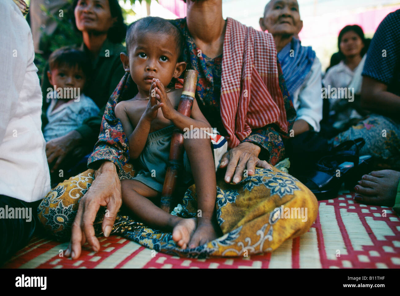 A thin and frail child sits on the lap of his mother among a crowd in ...