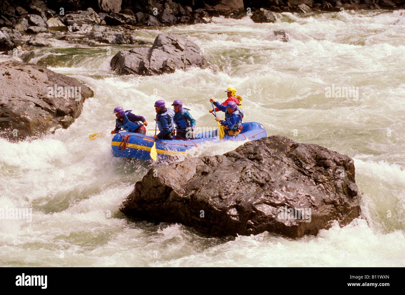 River rafters shoot the gap between two large boulders in roaring white ...