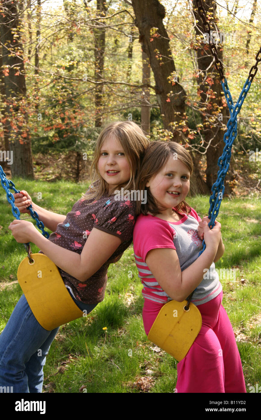 Two sisters smiling on swing in back yard Stock Photo - Alamy