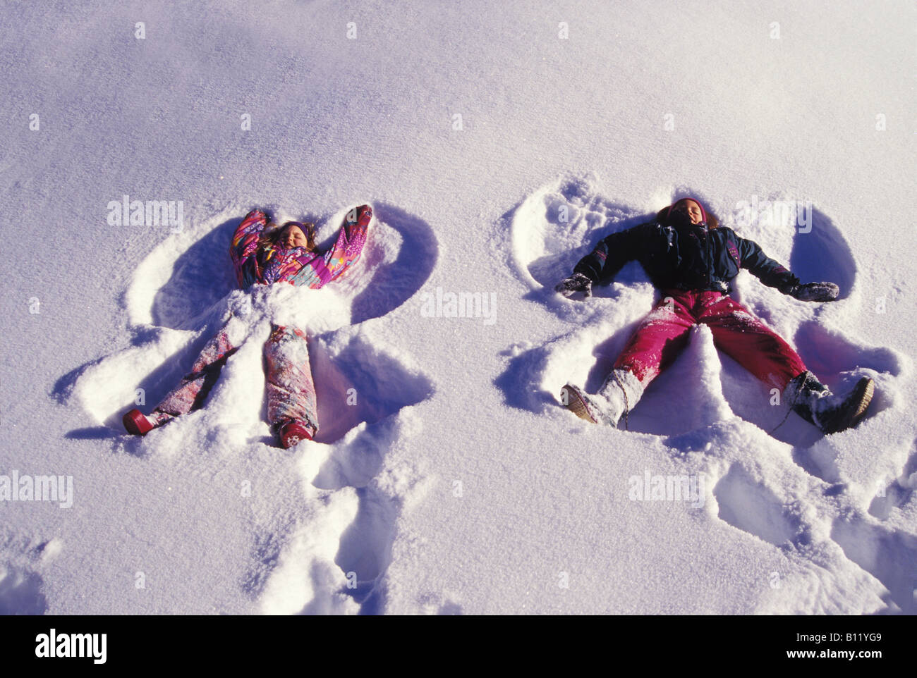 Two girls 8 and 9 years make snow angels in freshly fallen dry snow in ...