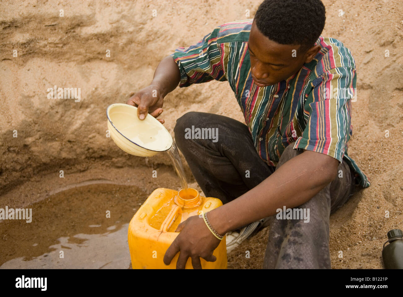 Young man pouring drinking water into a container from the water ...