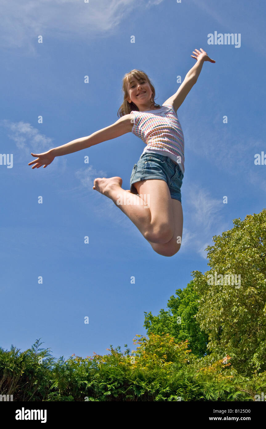A young girl (10 yrs) jumping from a trampoline in mid air on a bright ...