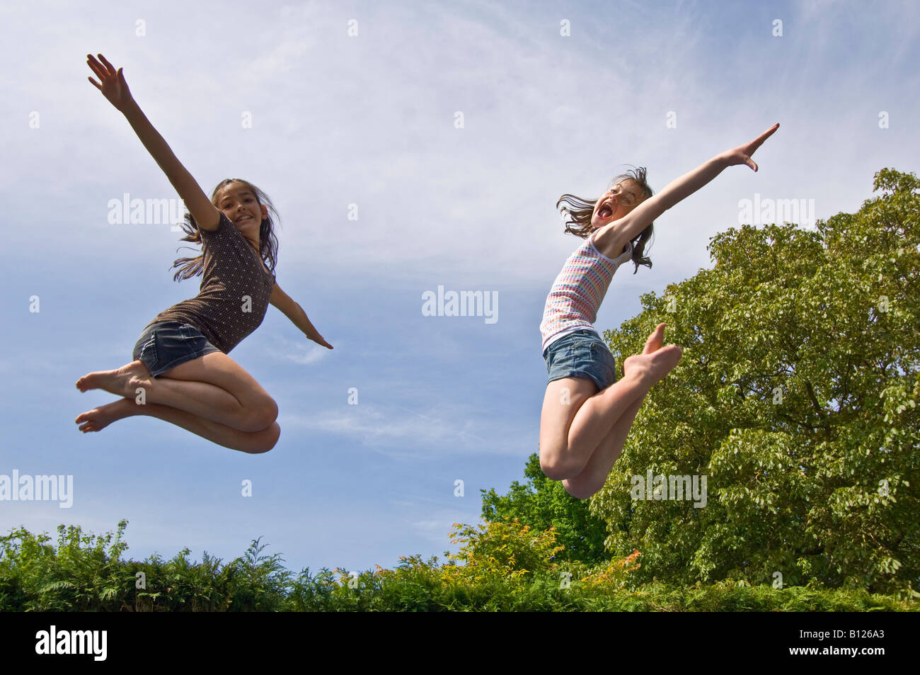 Two young girls (10 yrs) best friends, jumping from a trampoline in mid ...