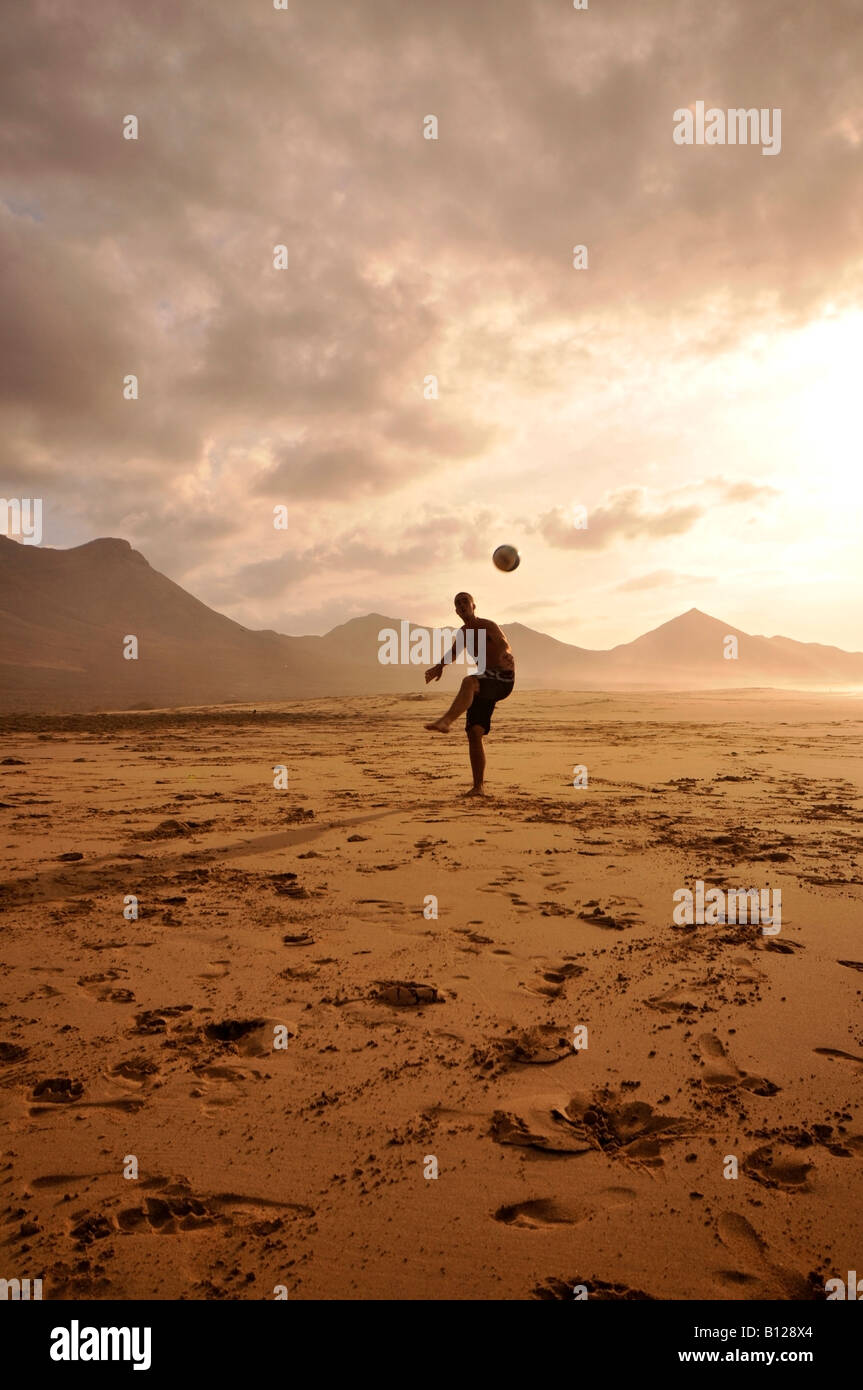 Silhouette of man playing football in the sand at a beach, backlight ...