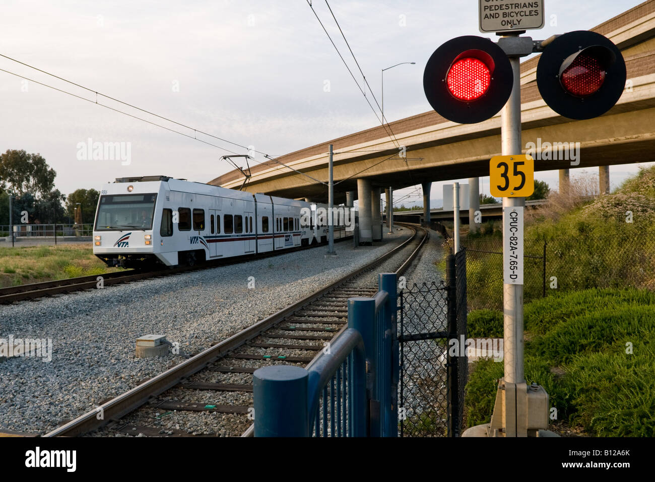 Urban light rail train enters a station from under a freeway overpass ...