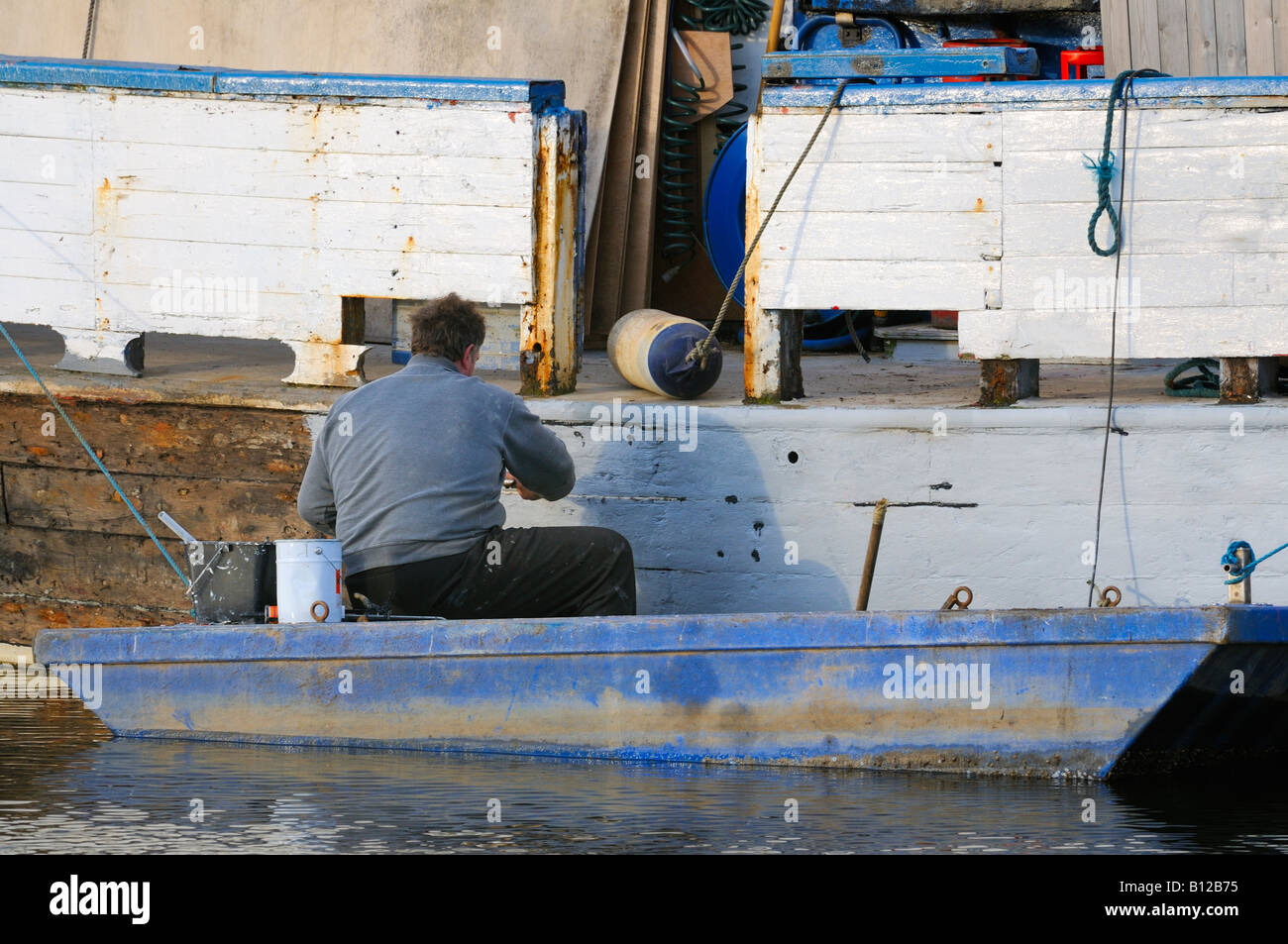 Man in a punt painting the hull of a small wooden trawler boat Stock ...