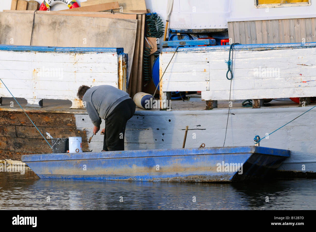Man in a punt painting the hull of a small wooden trawler boat Stock ...