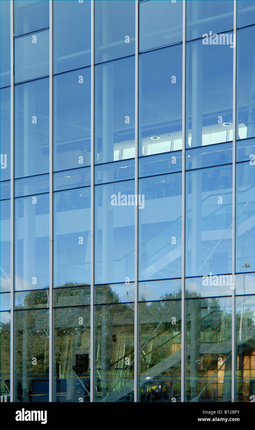 Modern glass fronted office building exterior with trees reflected on ...
