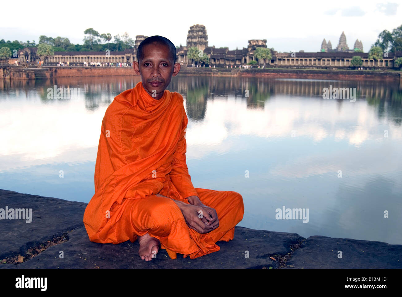 A Buddhist monk in a saffron robe sits serenely in front of Angkor Wat ...