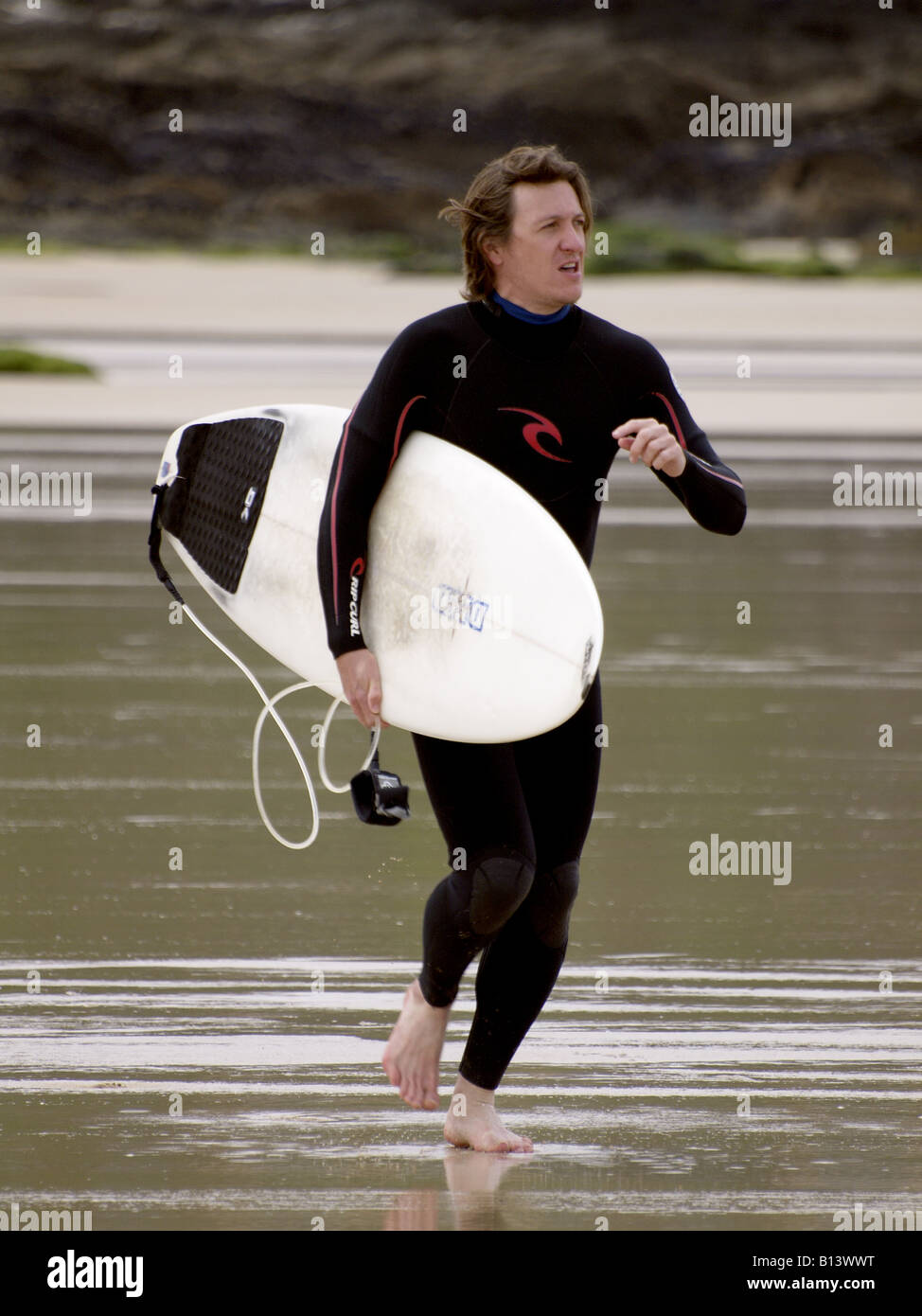 Surfer running along a sandy beach, with his surfboard under his arm ...